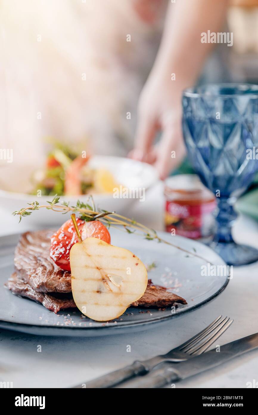 Fresh meat steak with pear and tomato decoration. Cutlery and wine ...