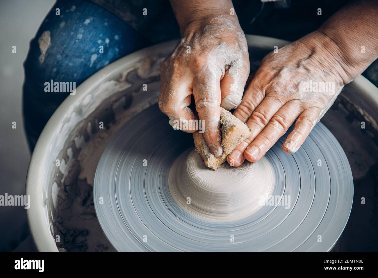 Wrinkled hands wizard on potter wheel makes clay dishes. Place to work ...
