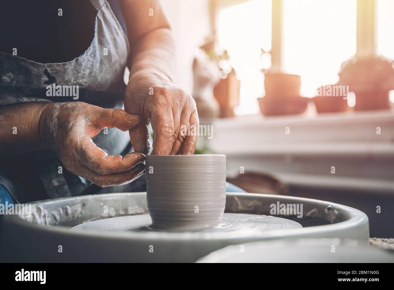 Wrinkled hands wizard on potter wheel makes clay dishes. Place to work ...