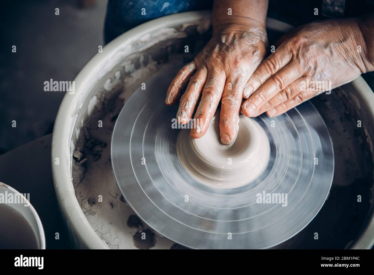 Wrinkled hands wizard on potter wheel makes clay dishes. Place to work ...