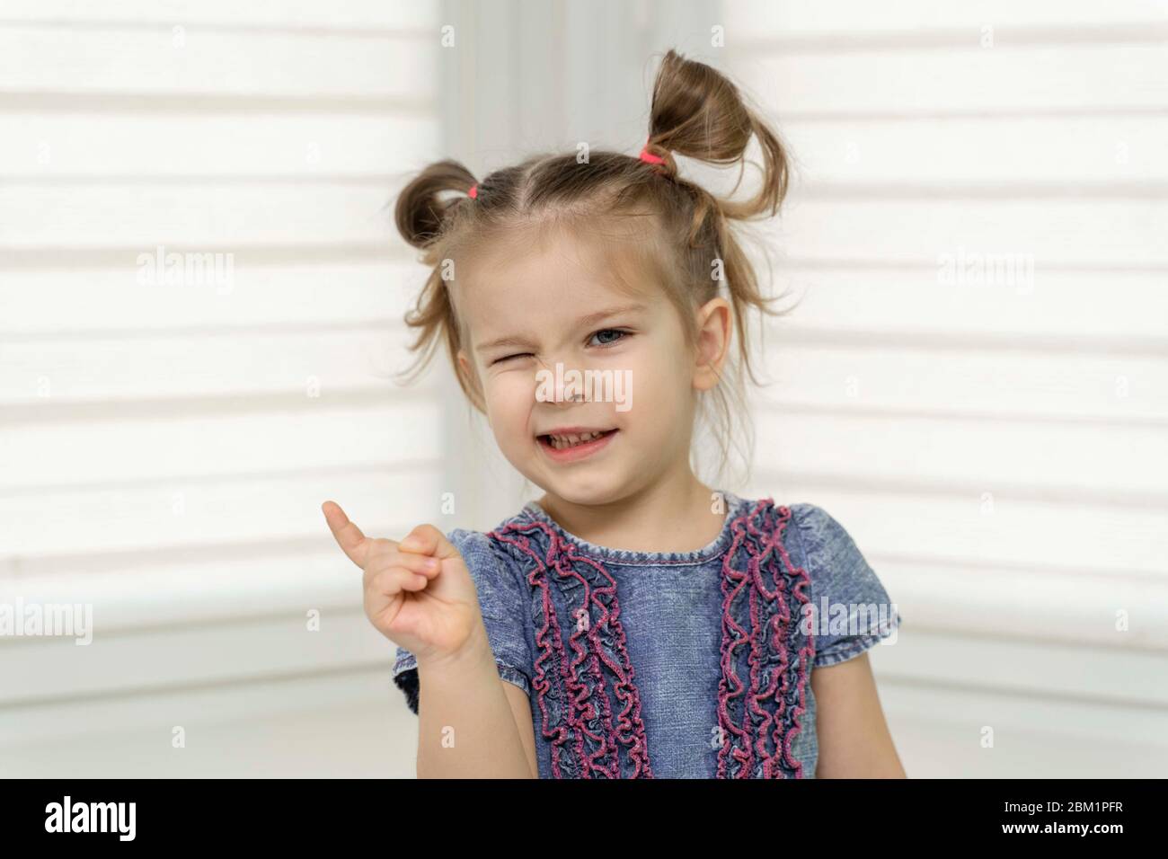 little girl 4 years old in a blue dress, playful face, narrowed eye ...