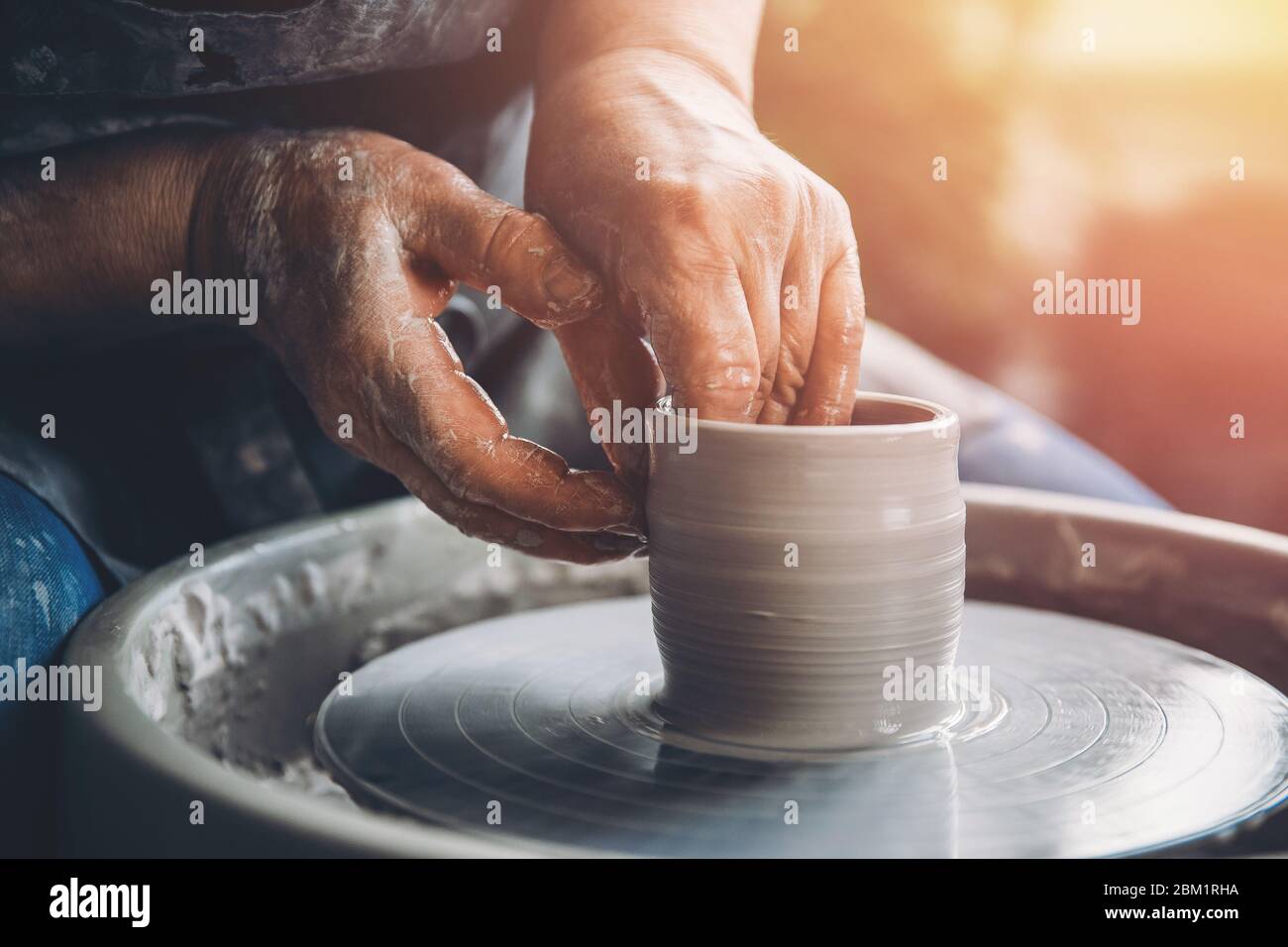 Wrinkled hands wizard on potter wheel makes clay dishes. Place to work ...