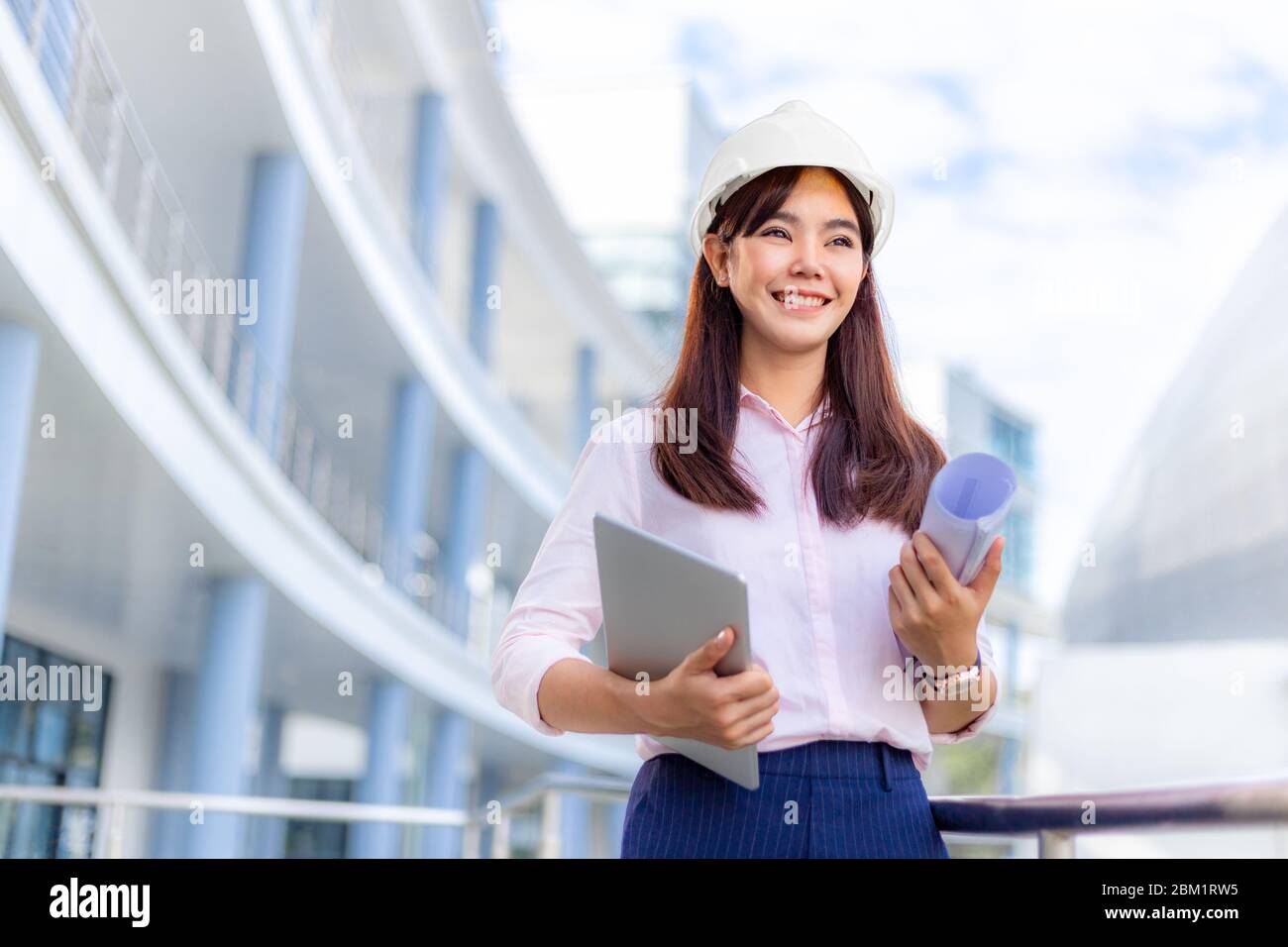 Happy young attractive female Asian engineer wearing hard hat holding ...
