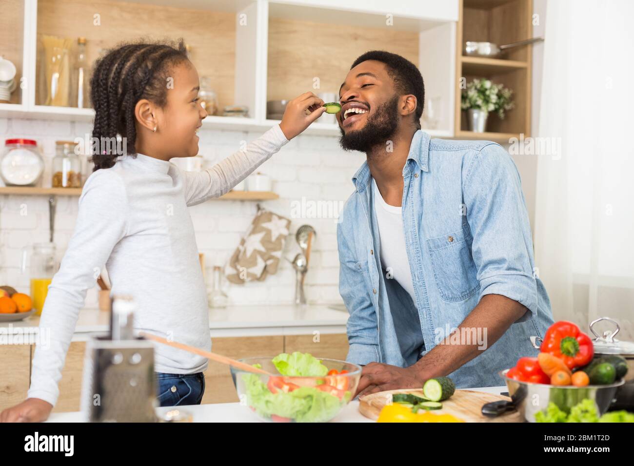 Cute little girl feeding her daddy while cooking Stock Photo - Alamy