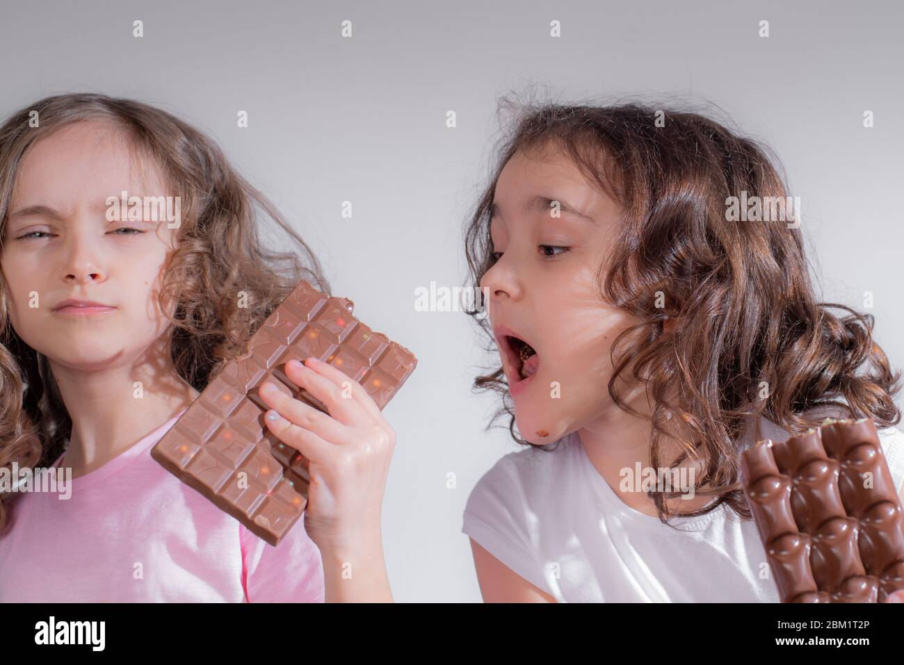 Children and chocolate.Two cheerful girls eat chocolate on a light ...
