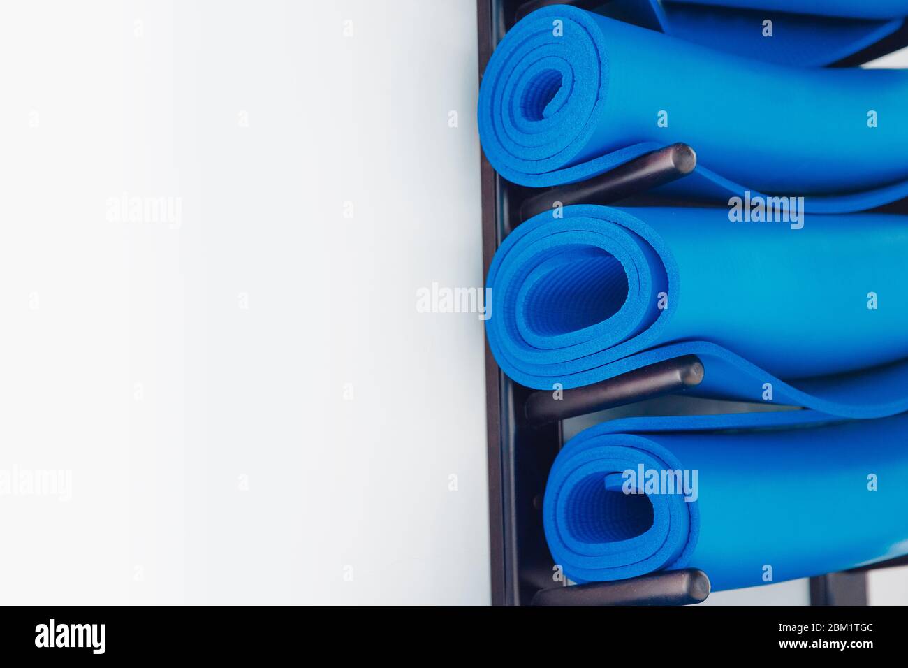 Blue yoga mat attached white wall in stack. Concept tool for practicing ...