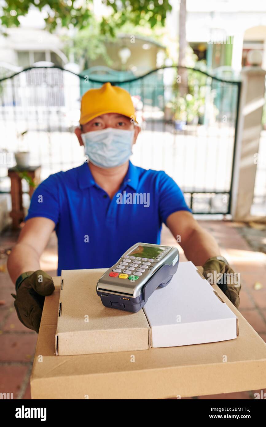 Delivery man in medical mask giving boxes with food and payment ...
