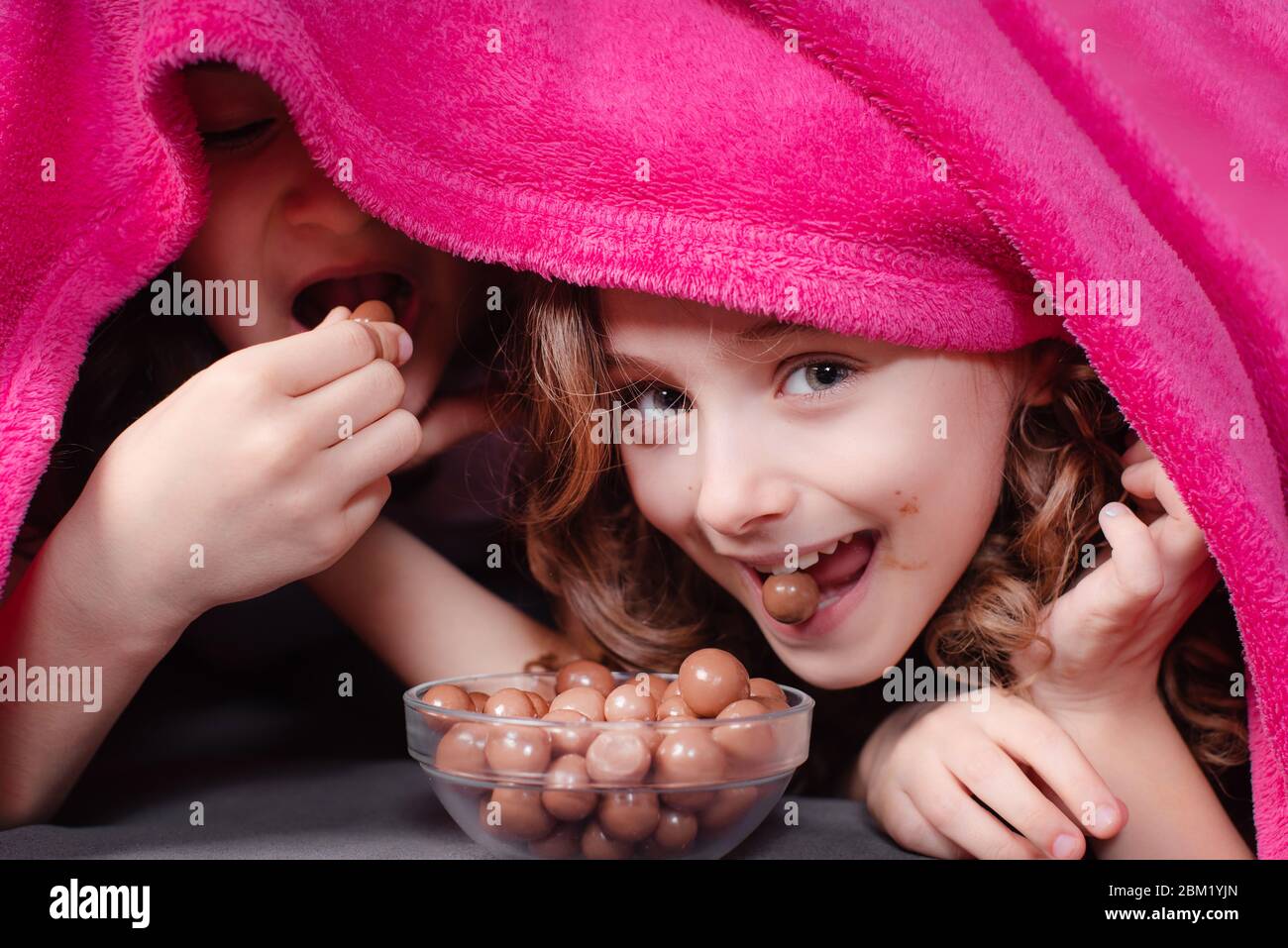 Children and chocolate.Two cheerful girls are sitting under the covers ...