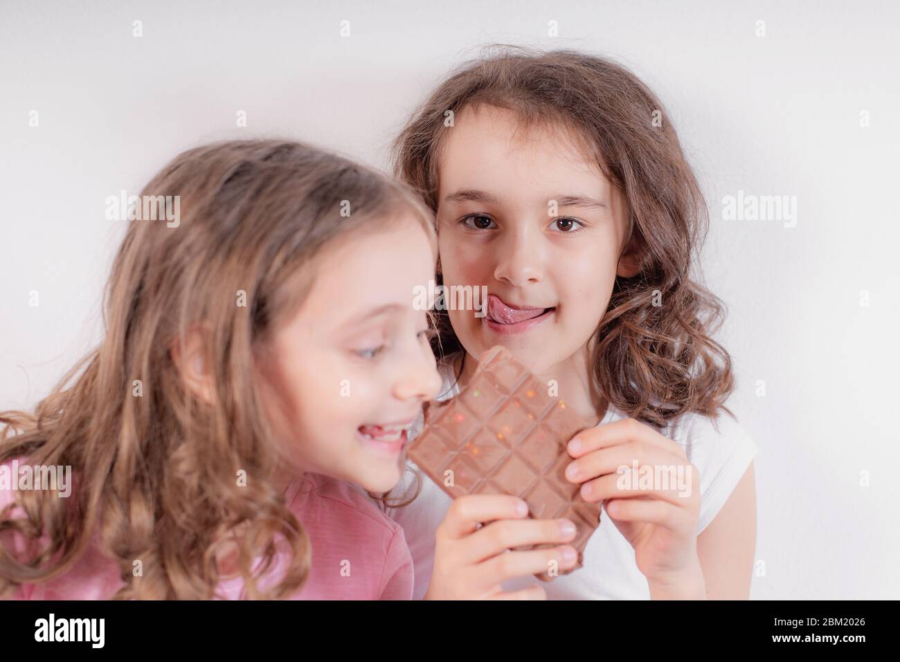 Children and chocolate.Two cheerful girls eat chocolate on a light ...
