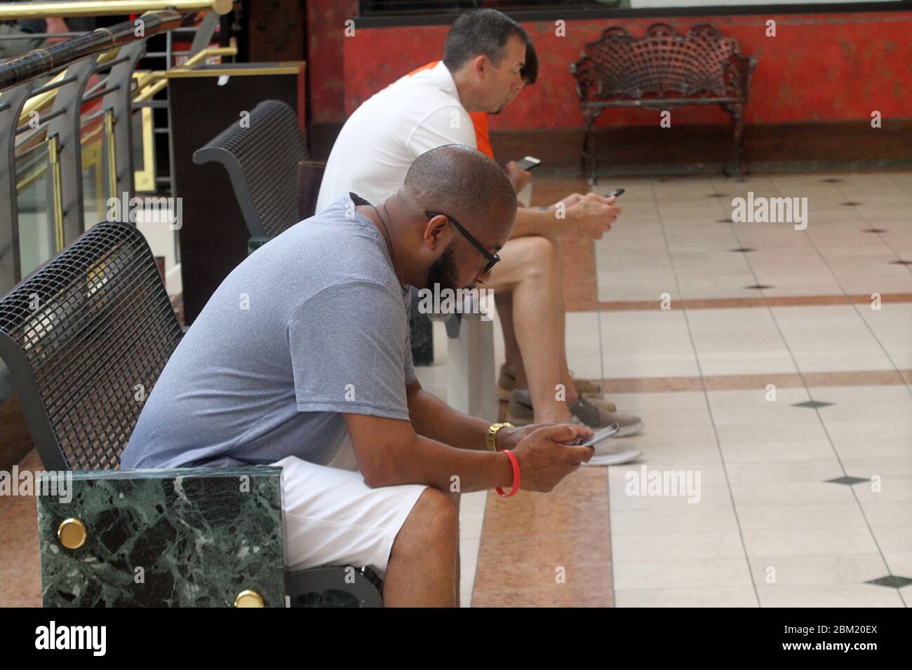 People using their iPhones while waiting on benches inside an American ...