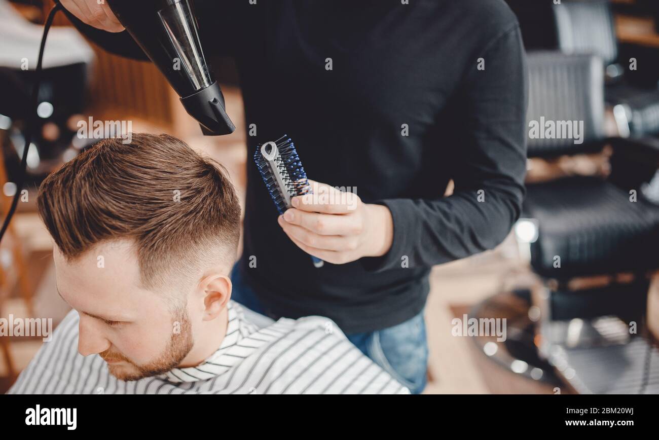Close-up master Barber does hairstyle and styling with dryer hair to ...