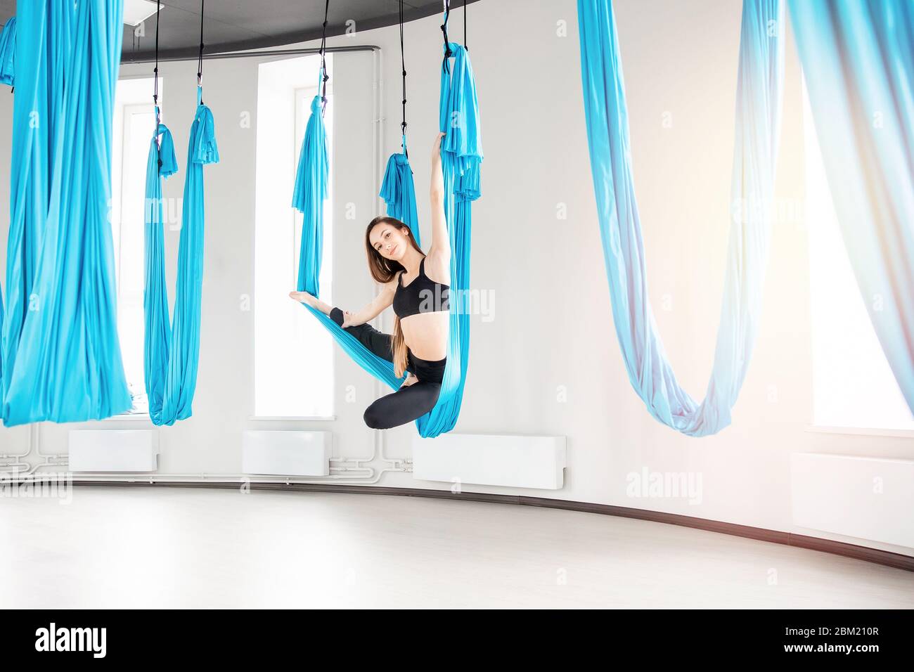 Aerial fly yoga in white gym, young gymnastics women in blue hammock ...