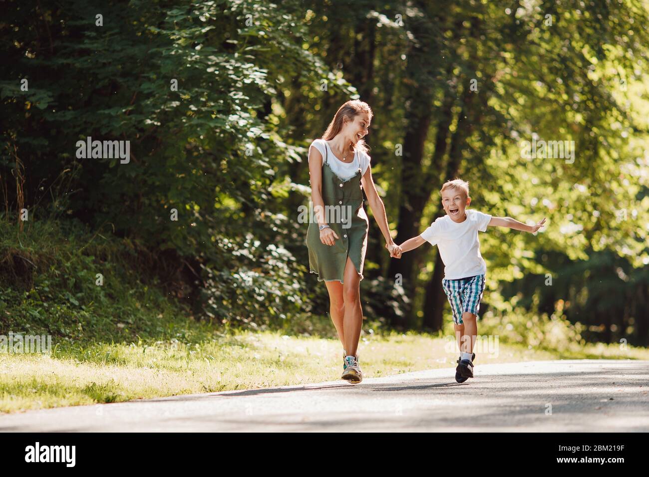 Sister teenager and little brother boy run their hands through park ...