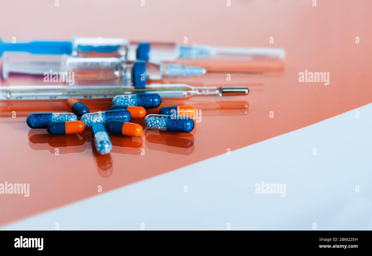 Thermometer and heap of pills, tablets, capsules on orange background ...