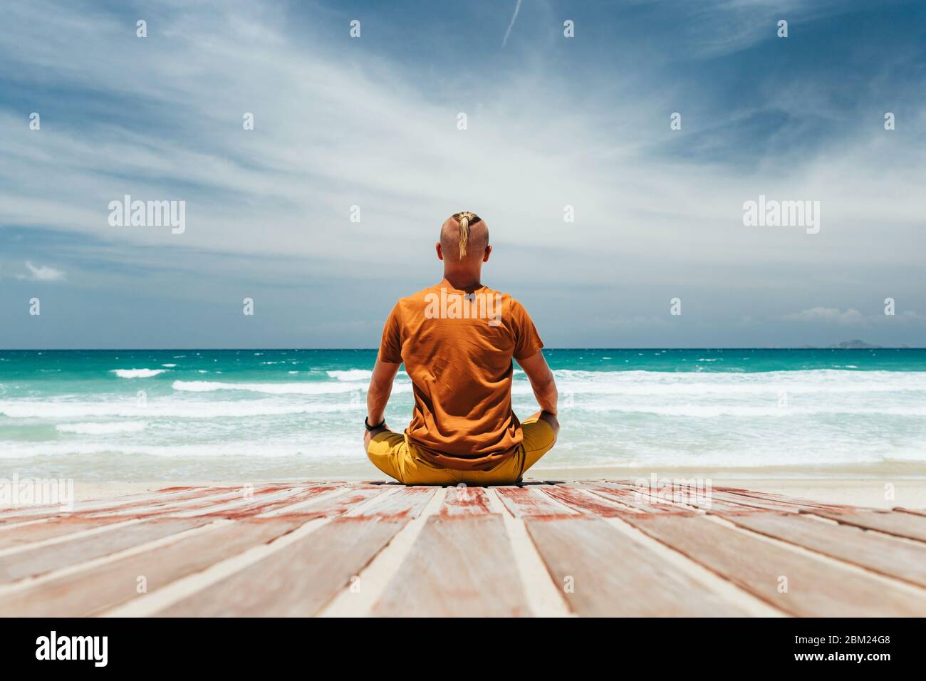 Young guy sits on the shore of a tropical beach The view from the back ...