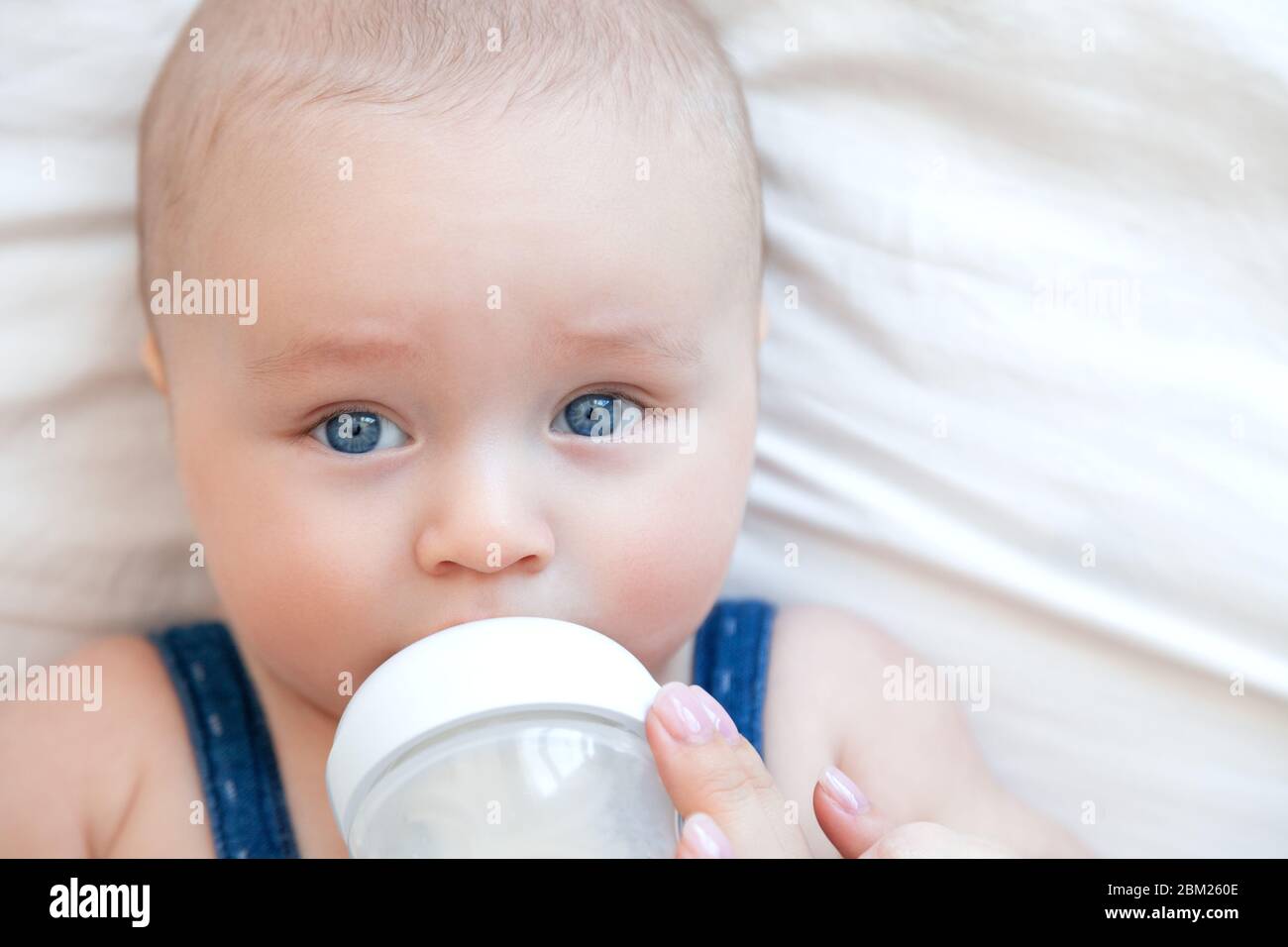 Beautiful baby eating milk from bottle in white bedroom on white ...