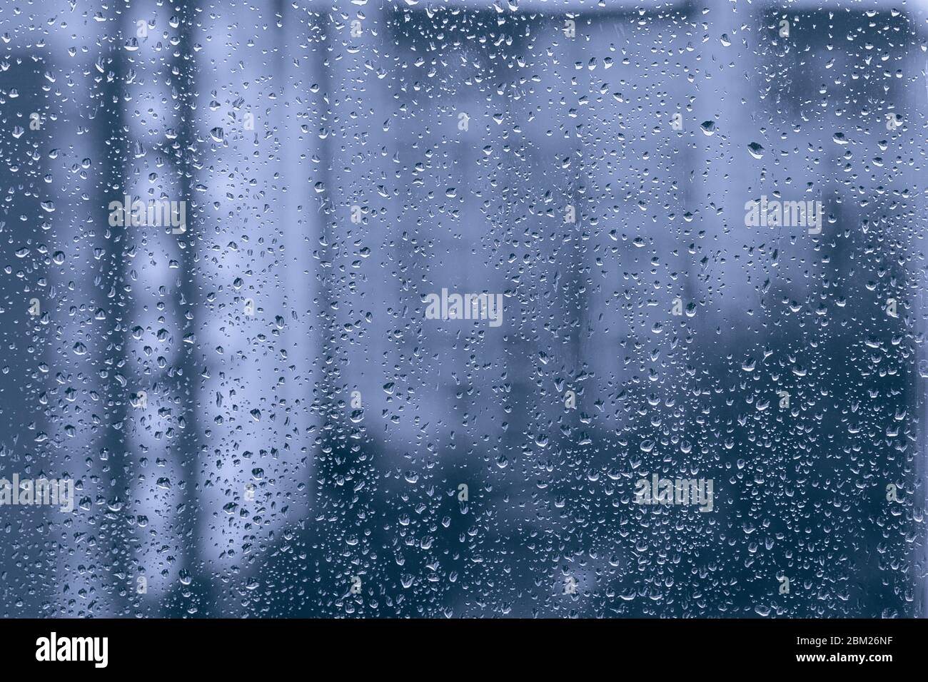 rainy droplets on a blue window glass transparent surface. drops on window shield in a rainy ...