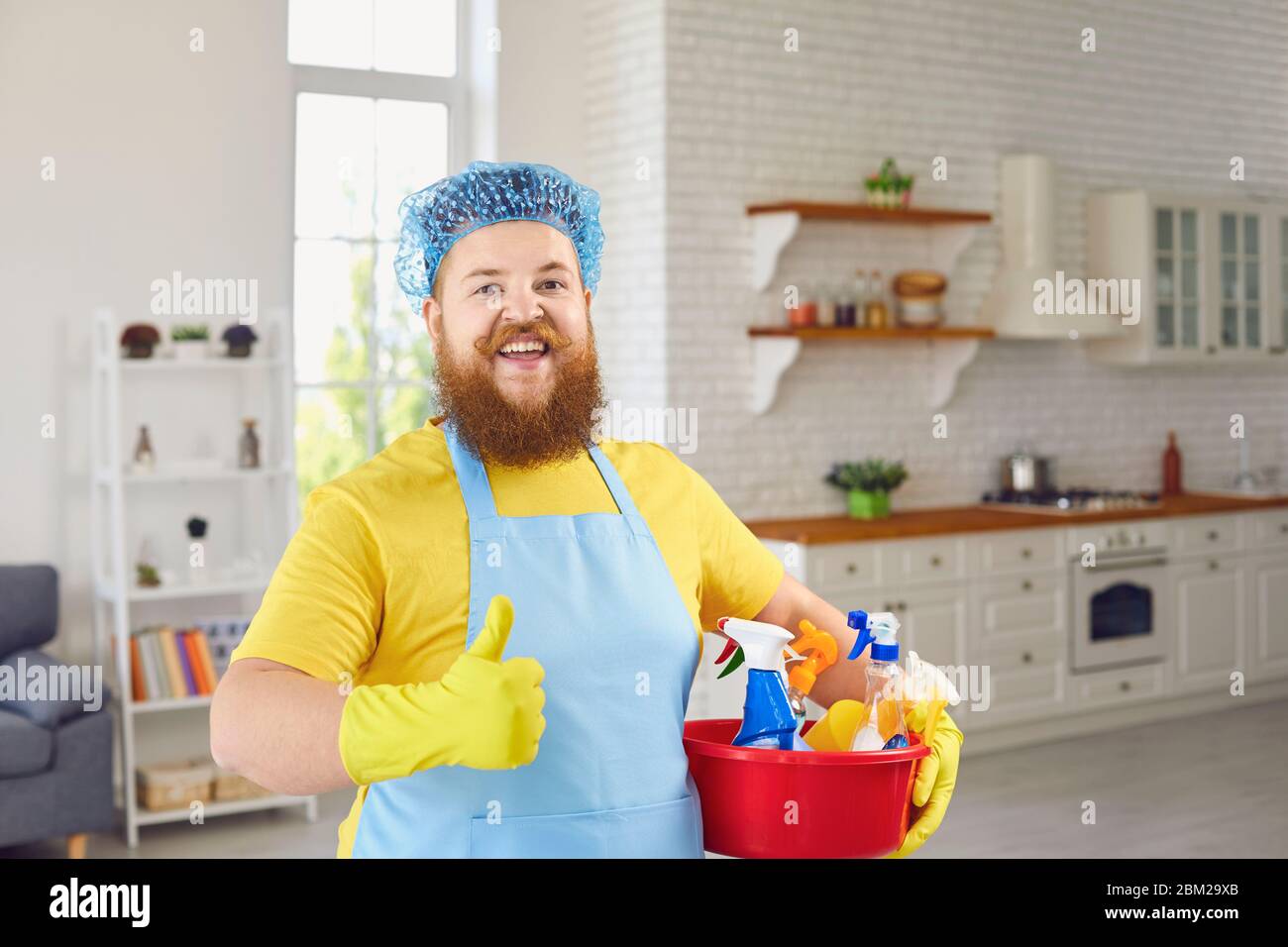 Funny fat man with a beard in an apron cleans the room in the house. A ...