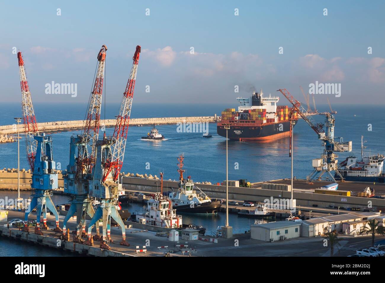 Dock with four-link cargo loading cranes and docked tugboats plus ...