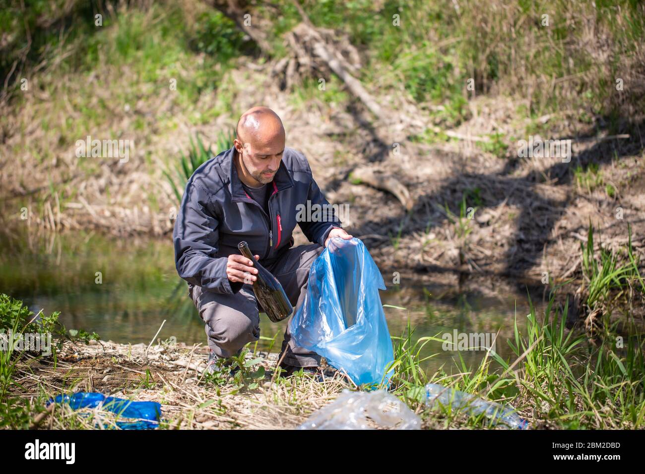 Man picking up plastic bottle, garbage collecting in the forest ...
