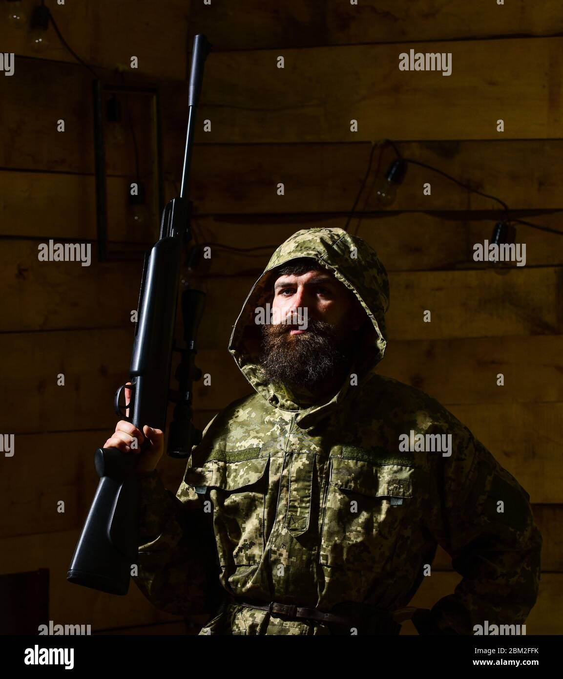 Man with beard wears camouflage hooded clothing, wooden interior ...
