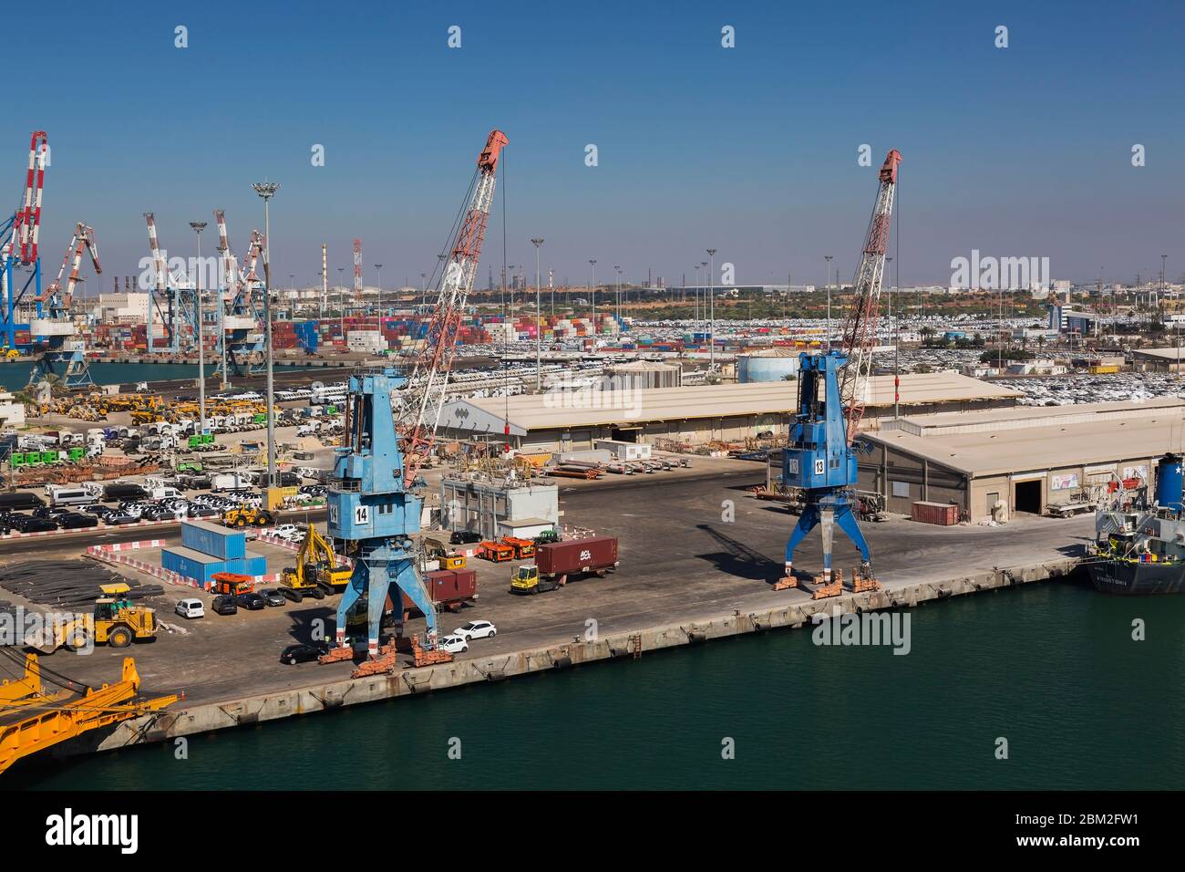 Four-link cargo loading cranes on dock with parked motor vehicles ready ...