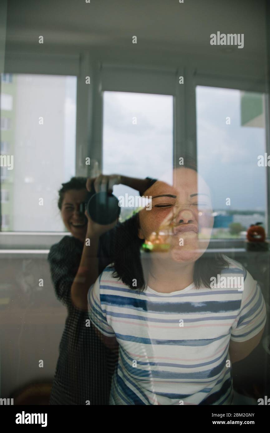 Young girl taking picture of her mother through the window. Woman ...
