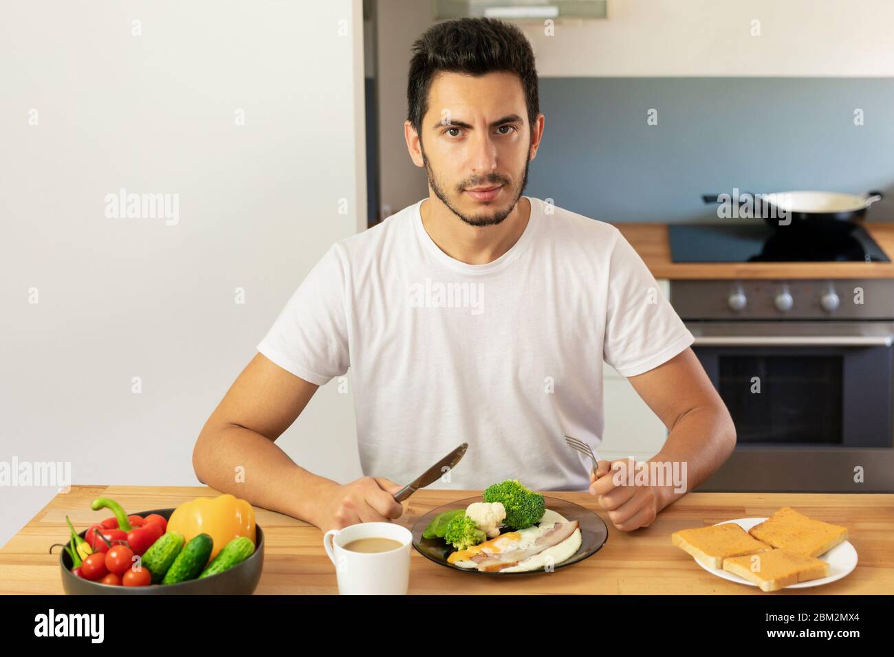A young man has breakfast at home in the kitchen. The guy eats toast ...