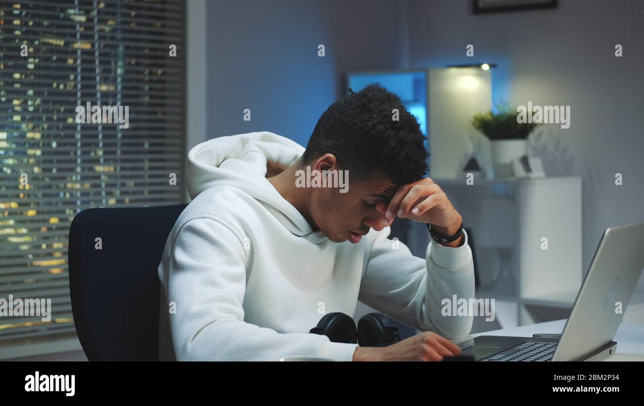 Sad black gamer in headphones lost online game on computer late at ...