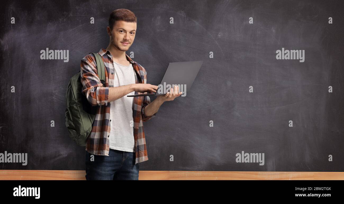 Male student working on a laptop computer and standing in front of a ...