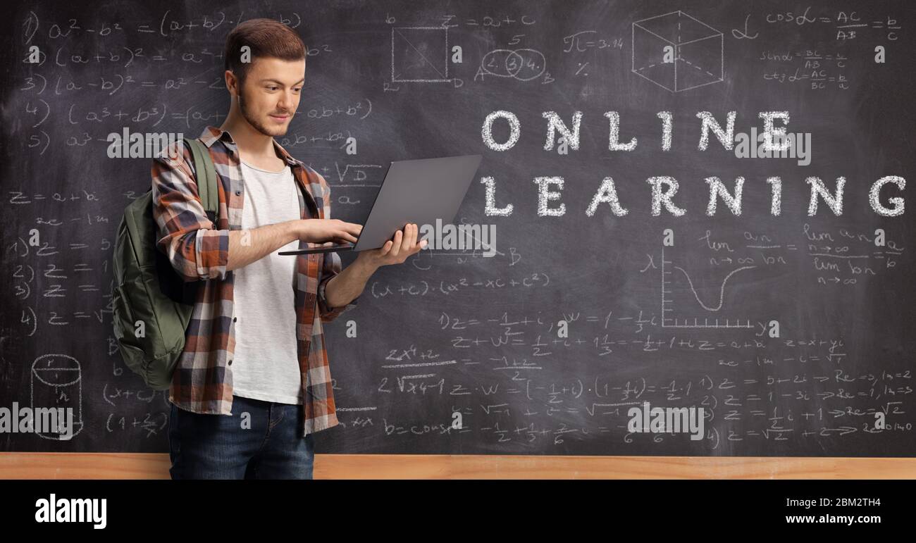 Male student with a laptop computer standing in front of a blackboard ...