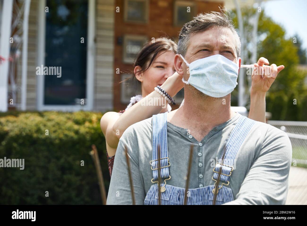 A wife ties a facemask on her husband before his workday to safeguard ...