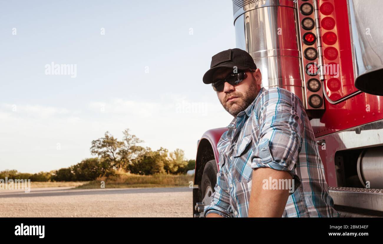Casual dressed trucker with plaid shirt and baseball cap sits next to ...