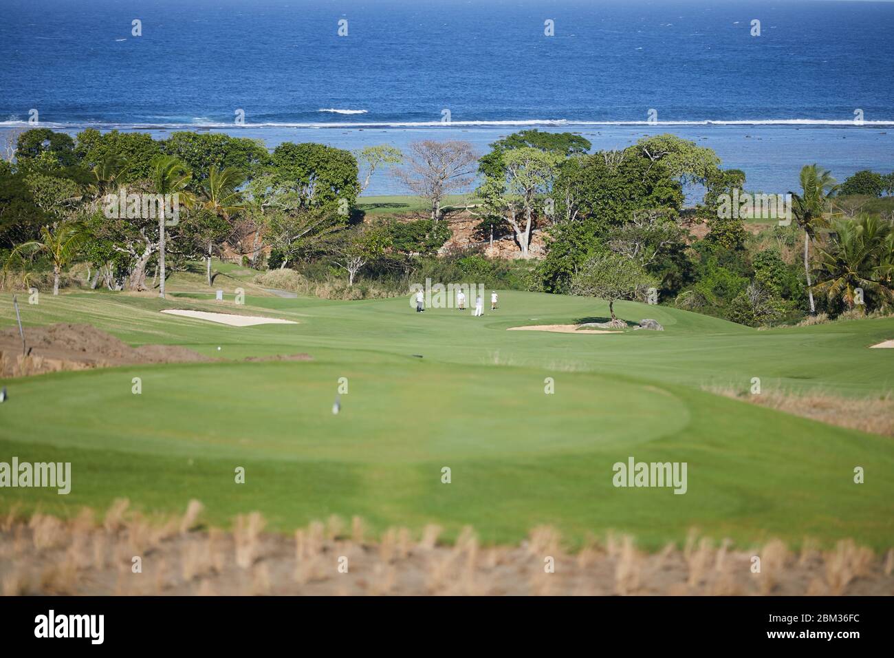 A golf course with pebble shore overlooks the ocean on the tropical ...