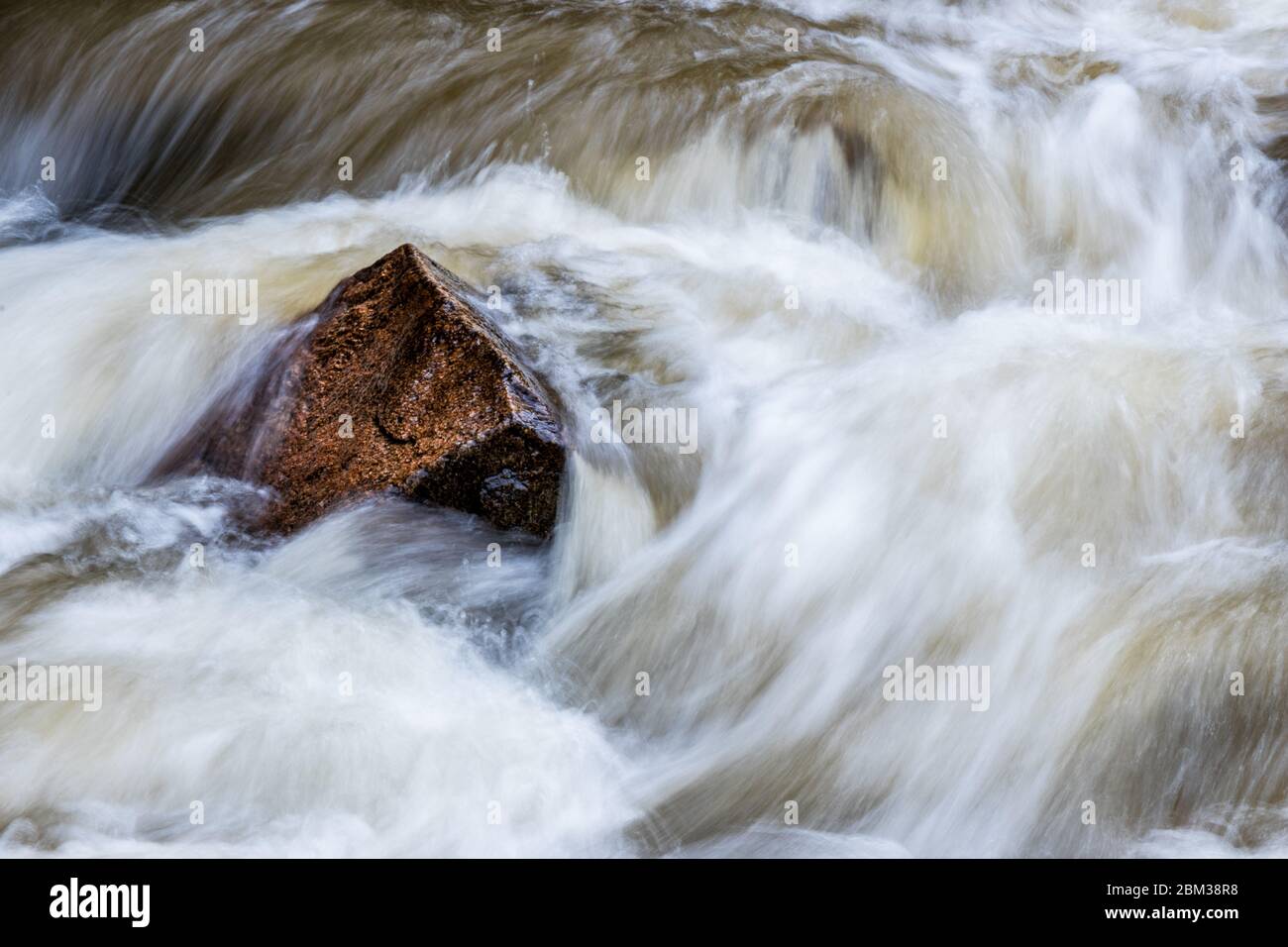 Rushing water around pointy rock Stock Photo - Alamy