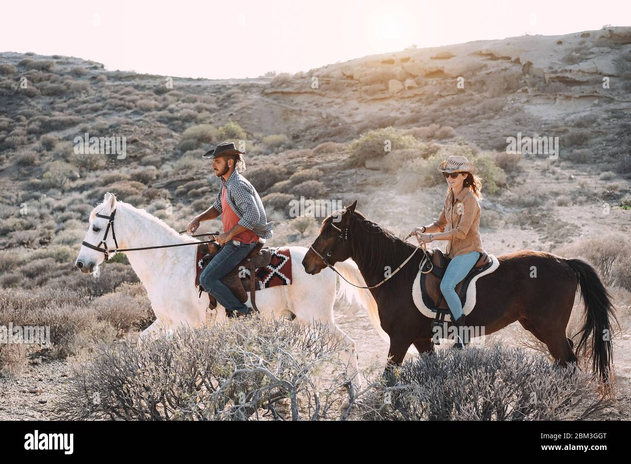 Young people riding horses doing excursion at sunset - Wild couple having fun in equestrian tour ...