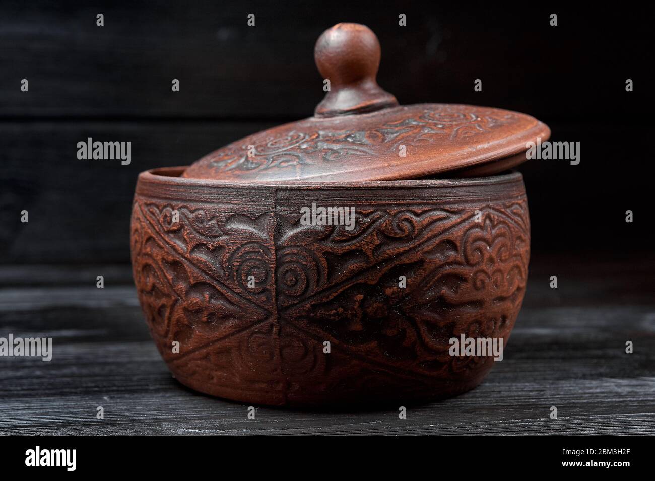 brown clay pan on a black wooden background with authentic carvings ...