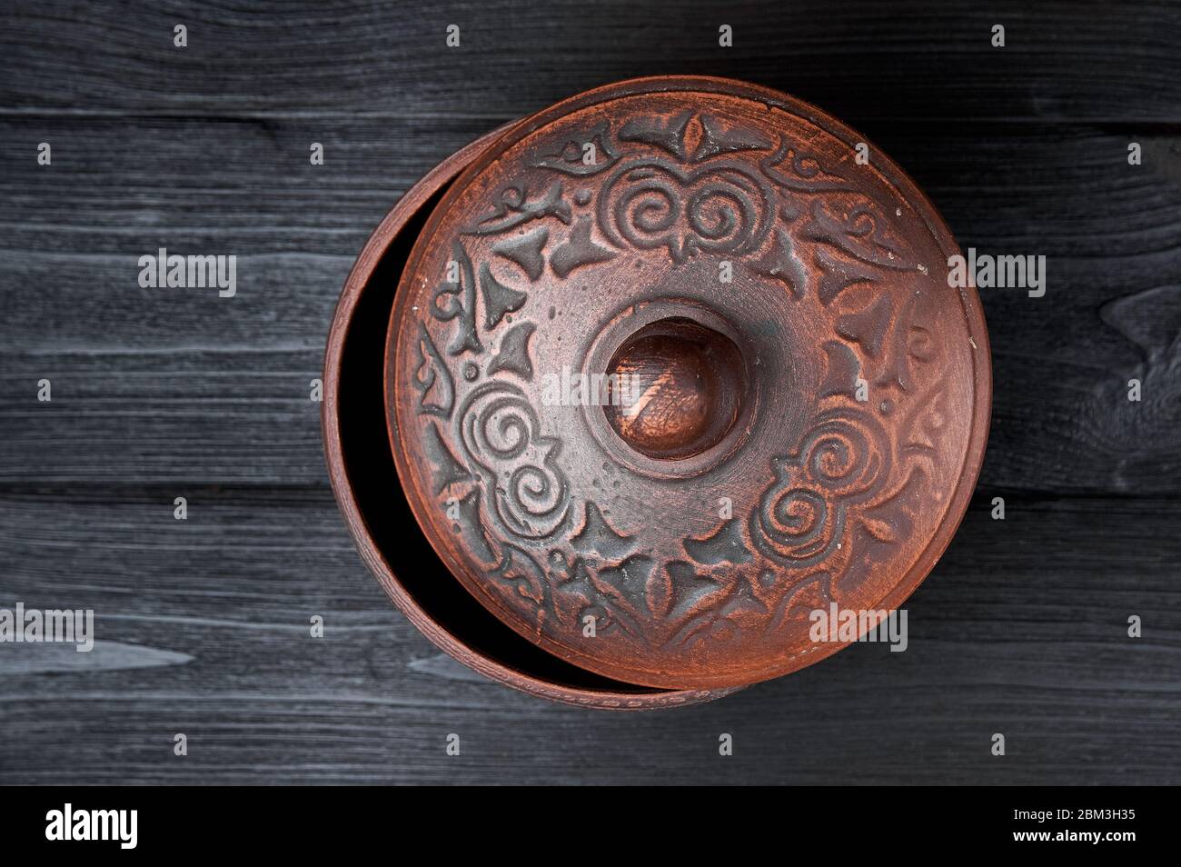 brown clay pan on a black wooden background with authentic carvings ...