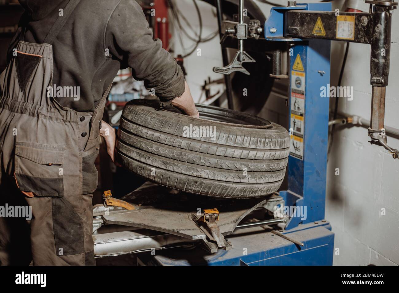 Car mechanic removing tire from rim with tire removal machinery ...