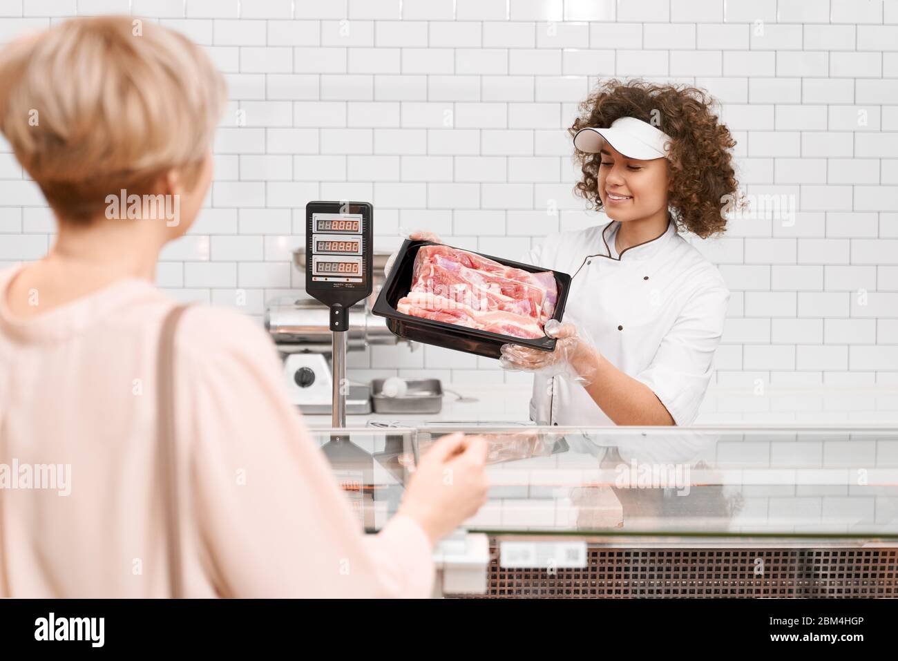 Young smiling woman with curly hair demonstrating to lady raw pork ...
