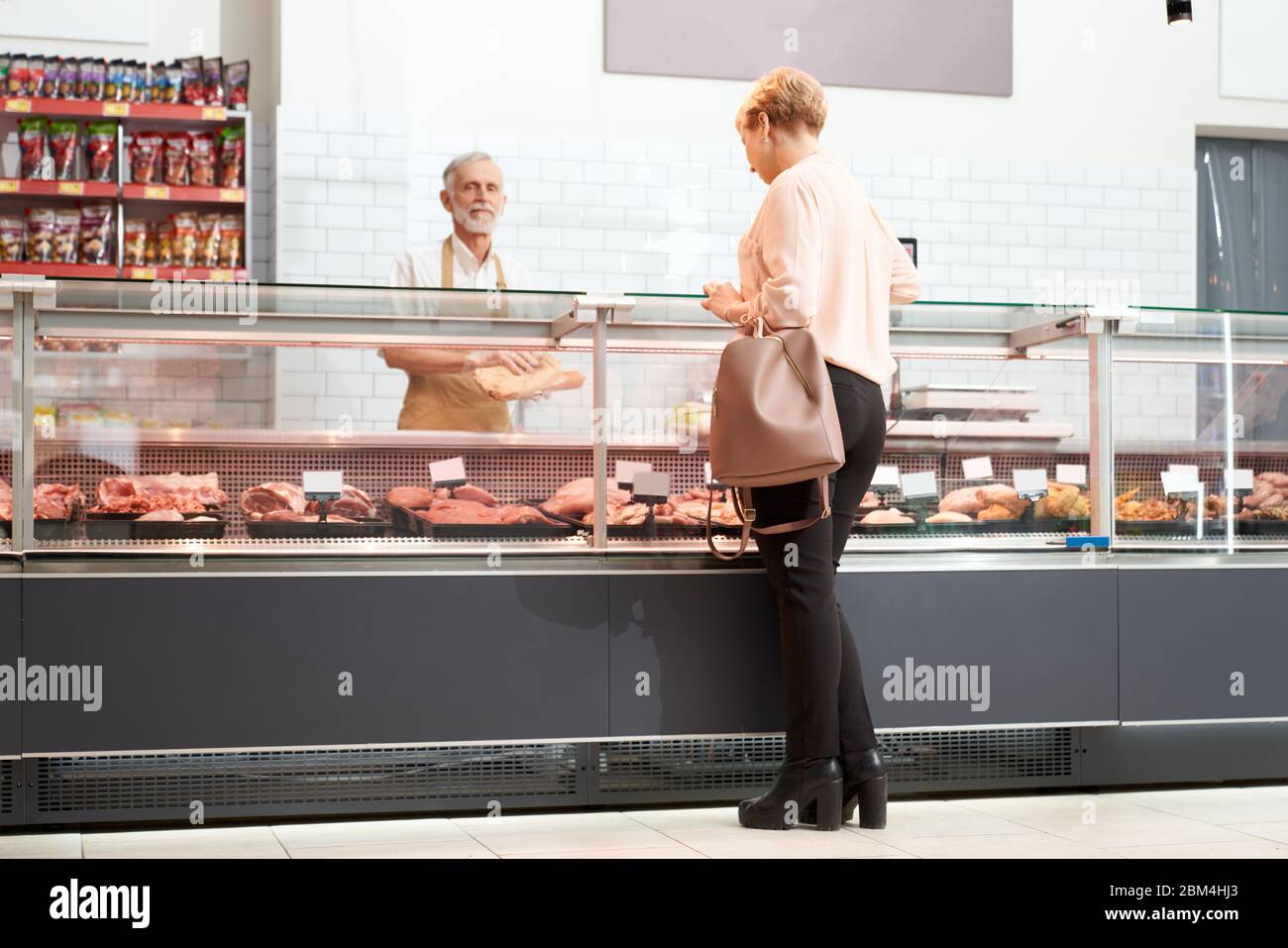 Back view of fasionable lady looking and choosing fresh meat in store ...