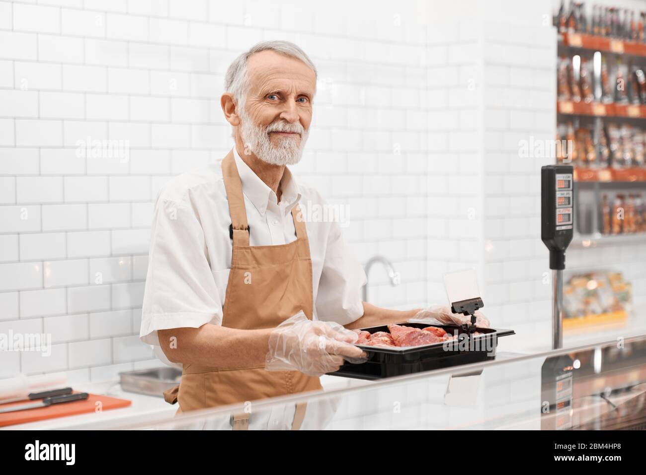 Portrait of smiling senior male butcher holding piece of fresh red raw ...