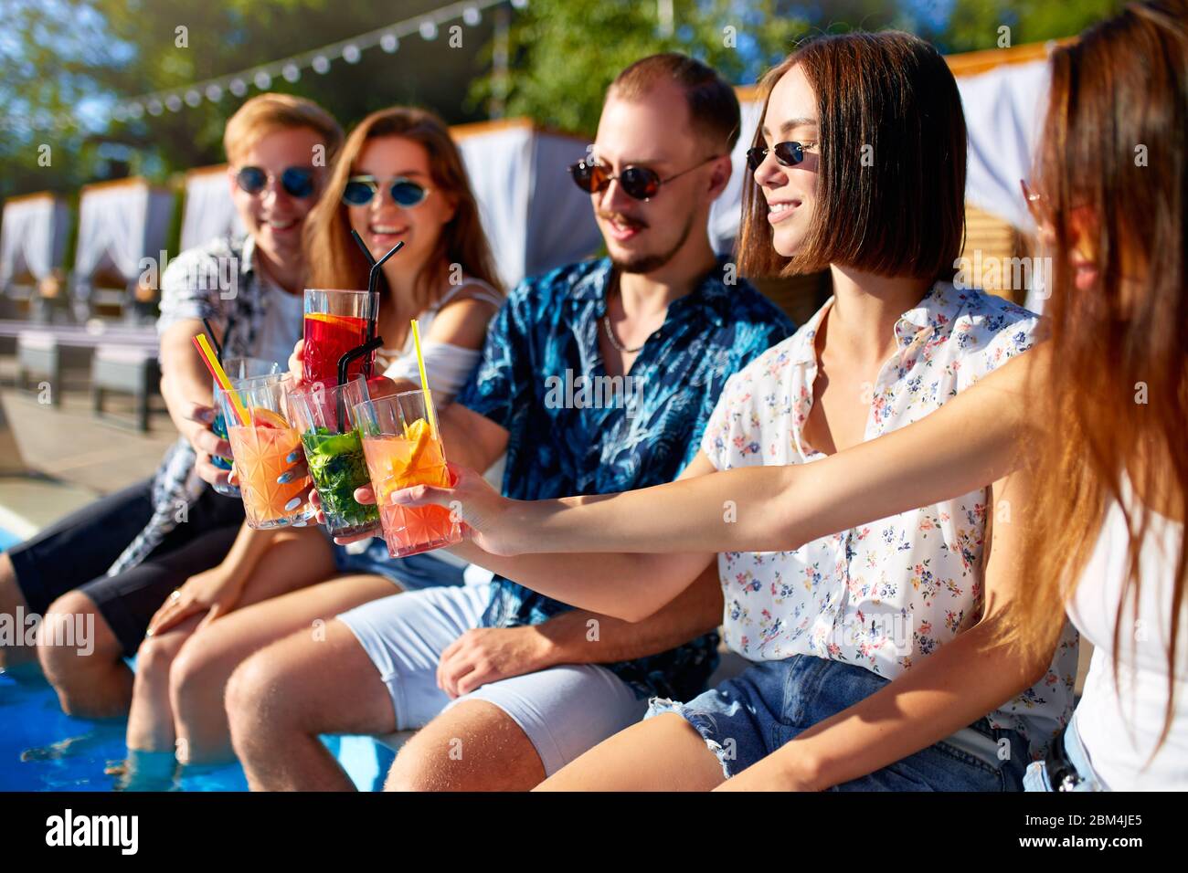 Group of friends having fun at poolside party clinking glasses with ...