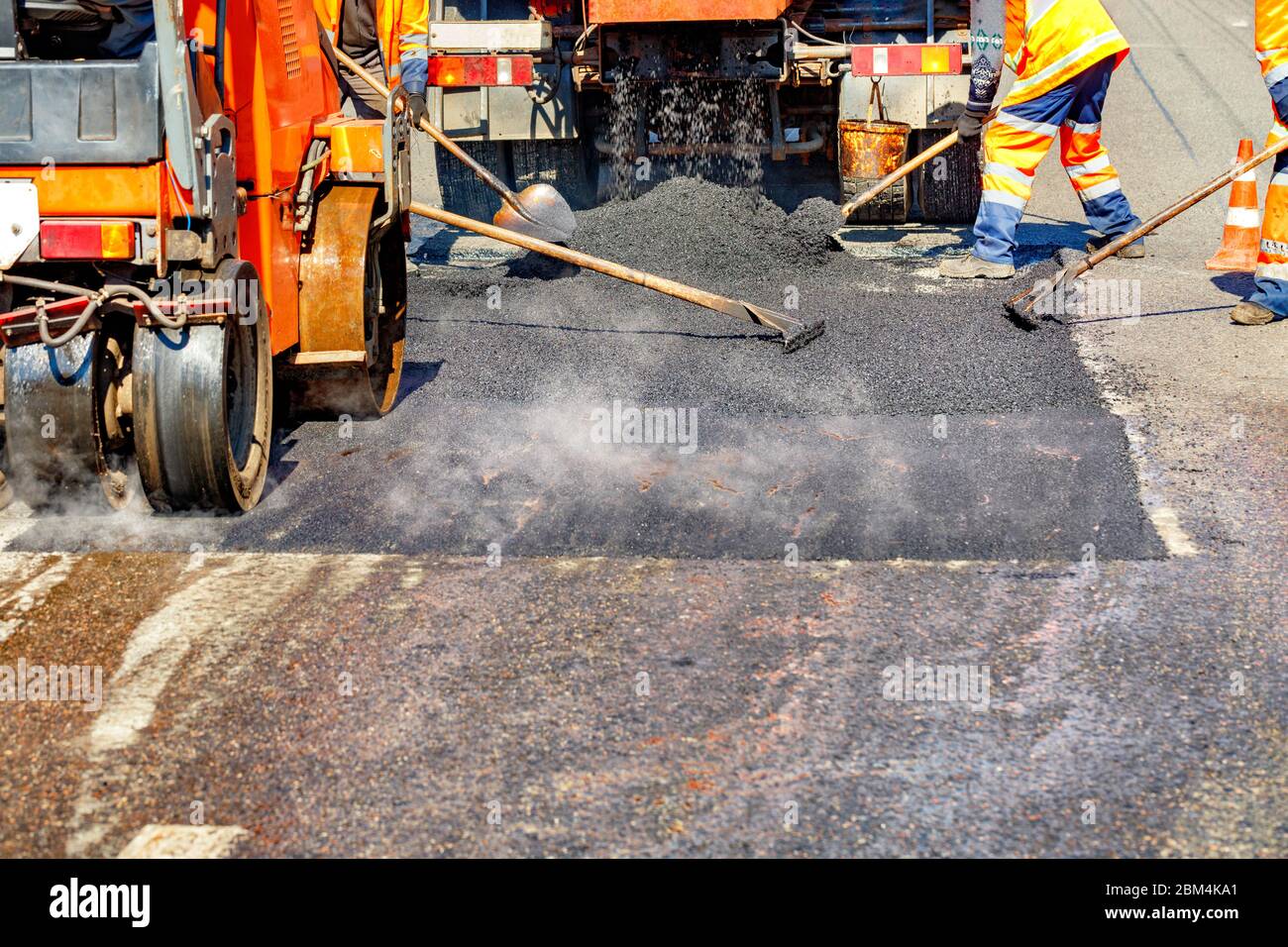 A team of road workers in protective orange overalls repairs a section ...