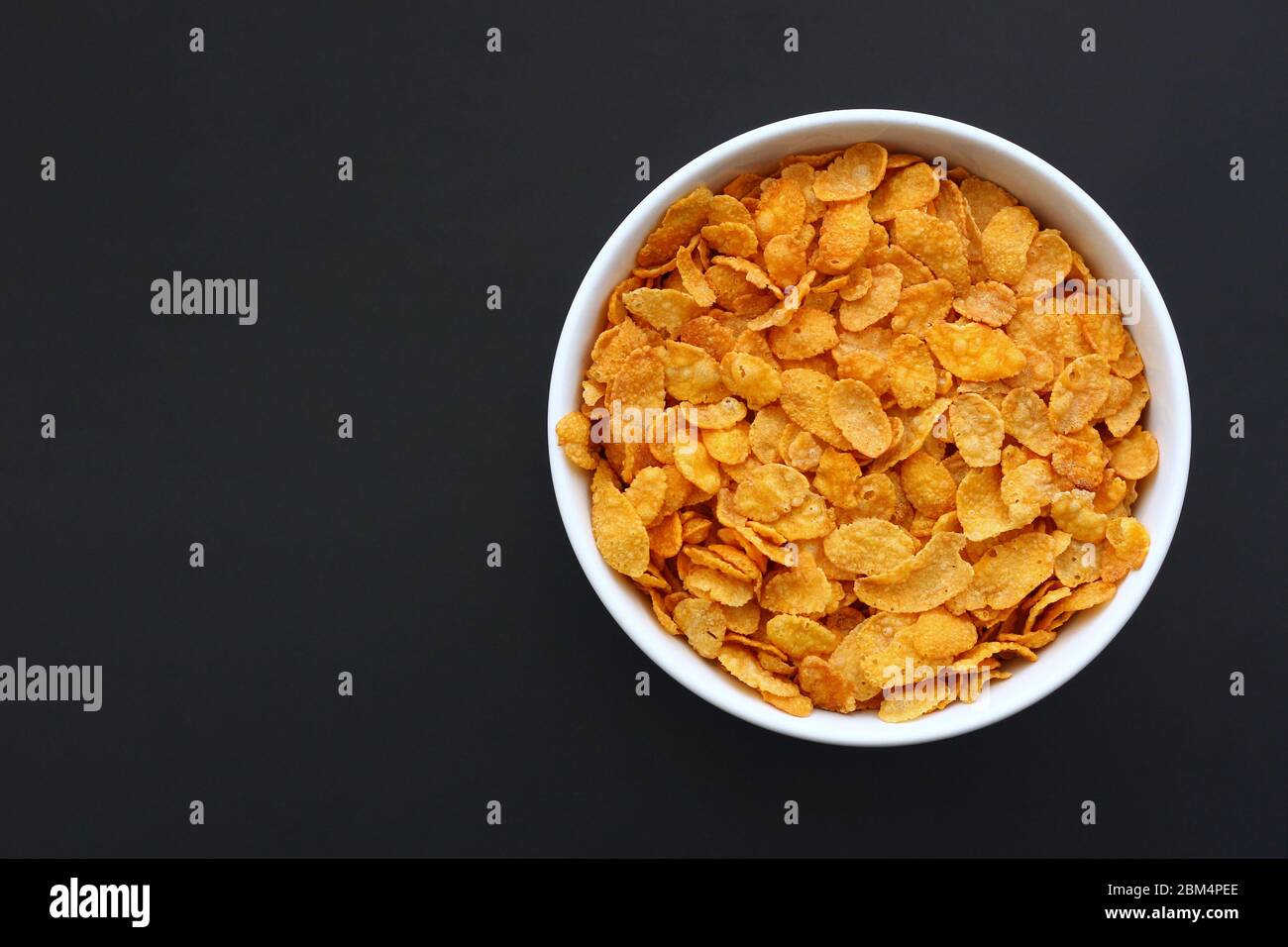 Dry corn flakes in a white bowl on a black metallic surface. Copy space ...