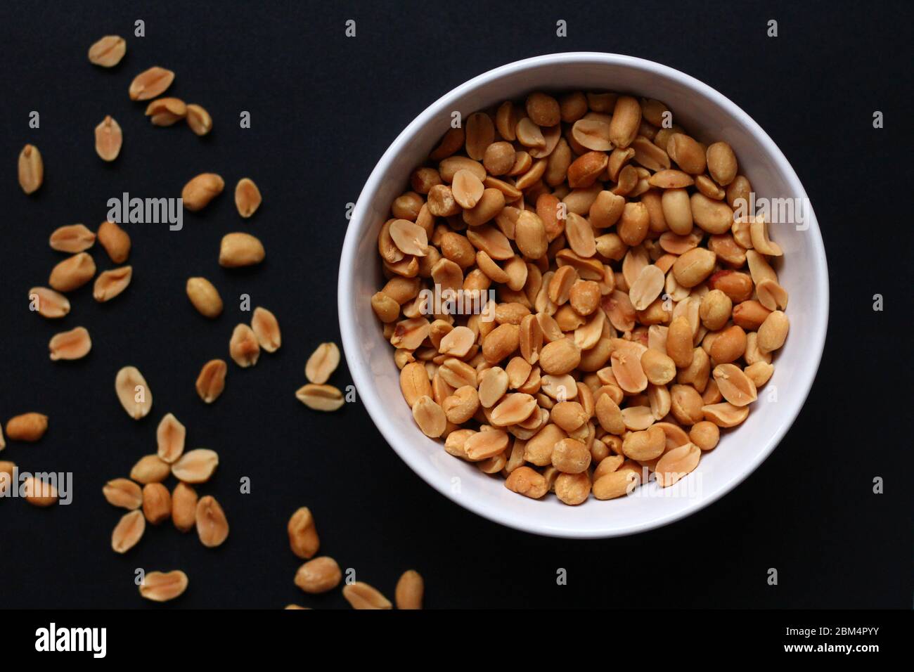 Peanuts in a white bowl as seen from above with some peanuts spreaded ...