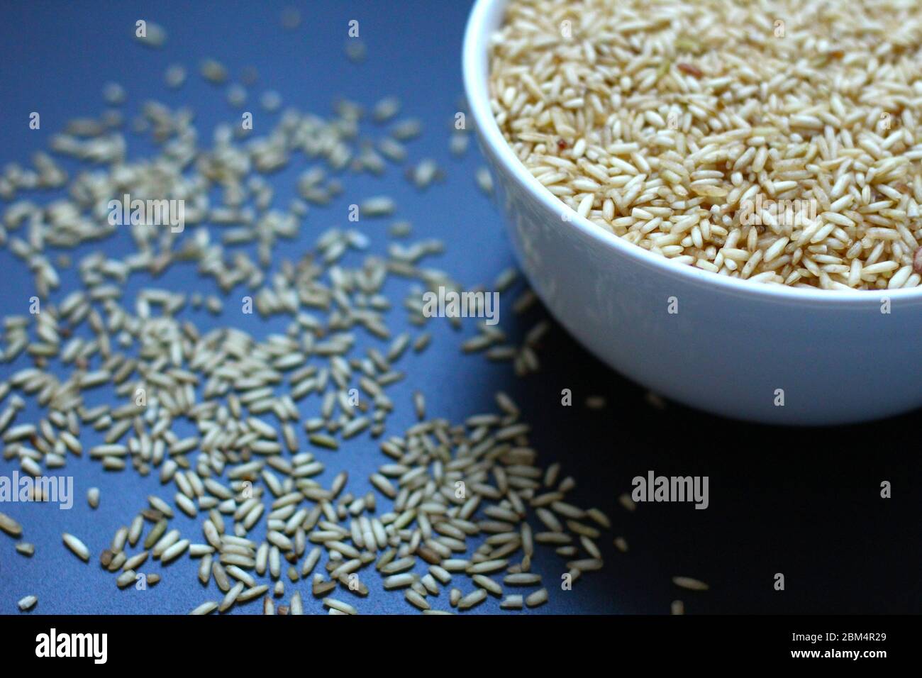 Rice, uncooked, in a white bowl on a black surface with rice spreaded ...
