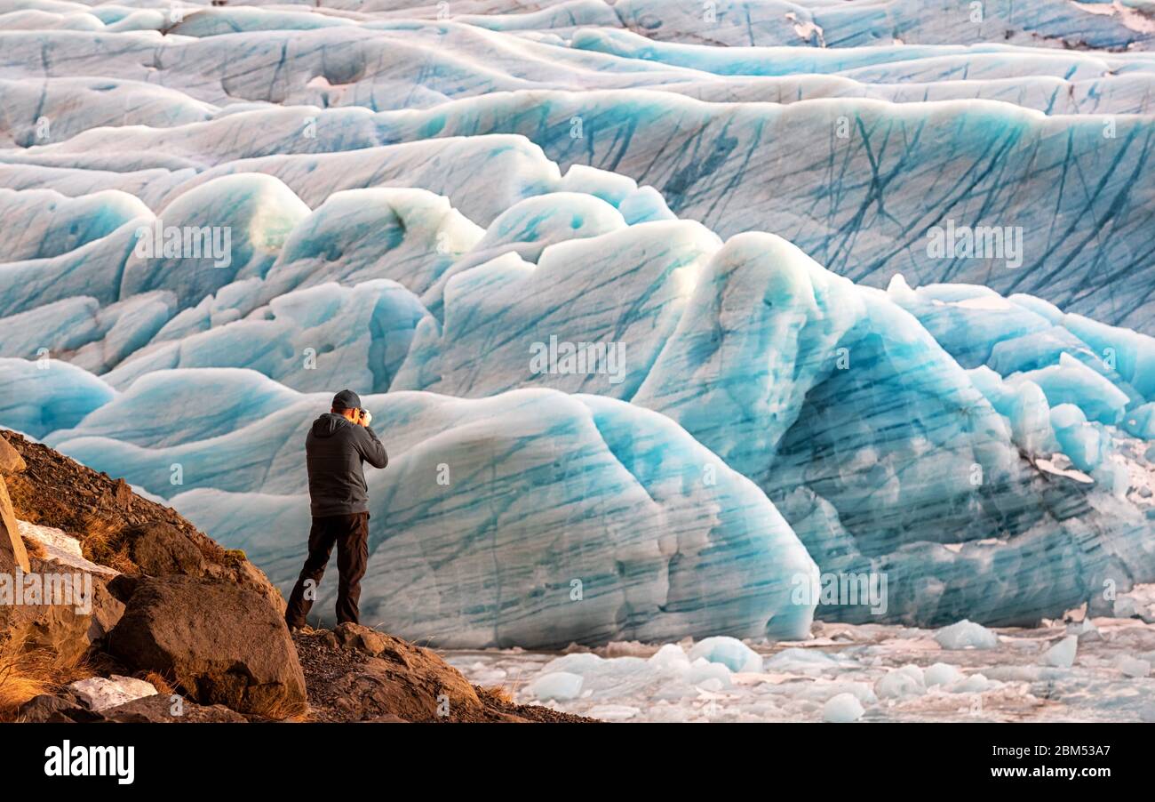 Man photographs the blue glacial ice at the Svinafellsjokul glacier in ...