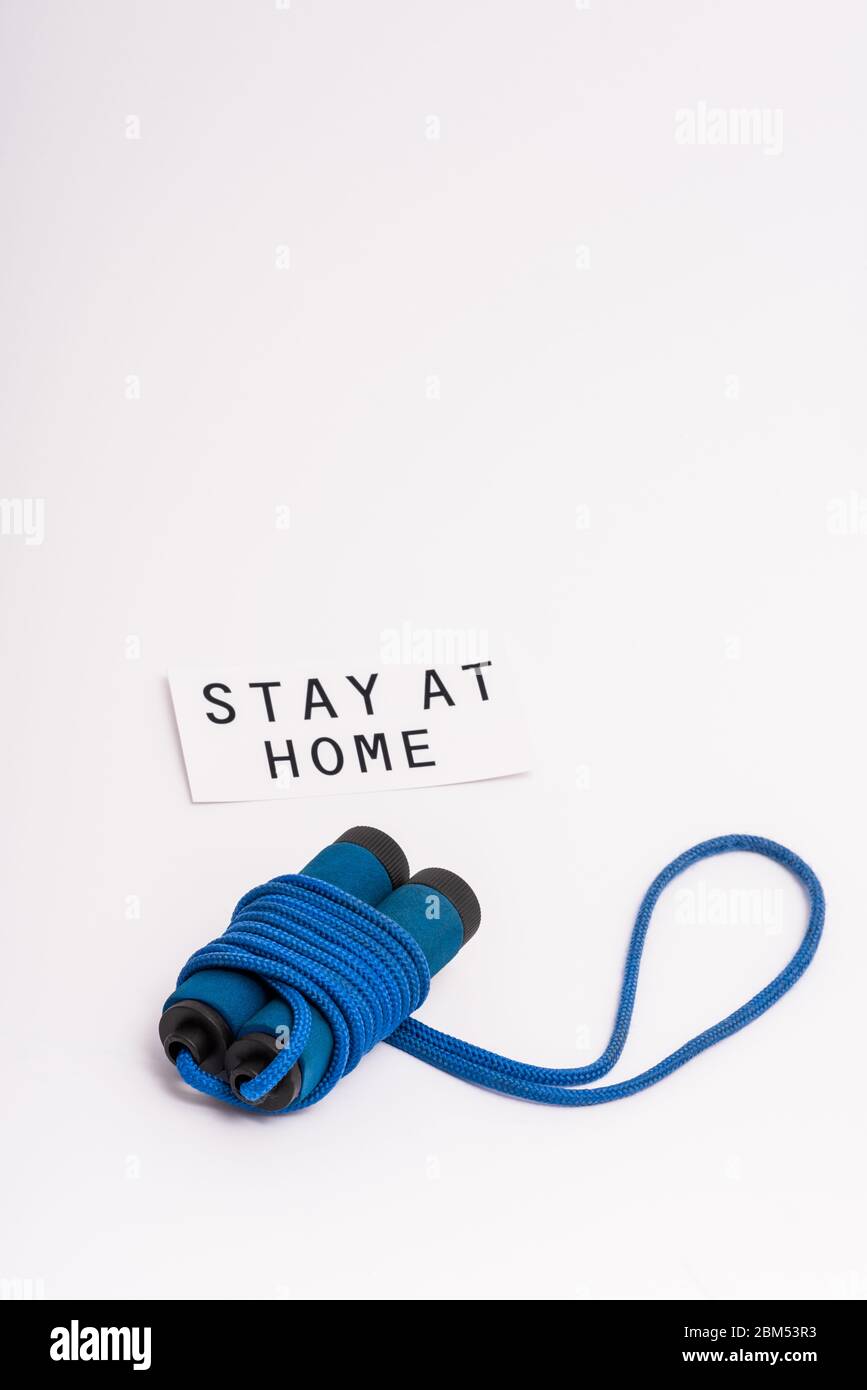 blue skipping rope near paper with stay at home lettering on white ...