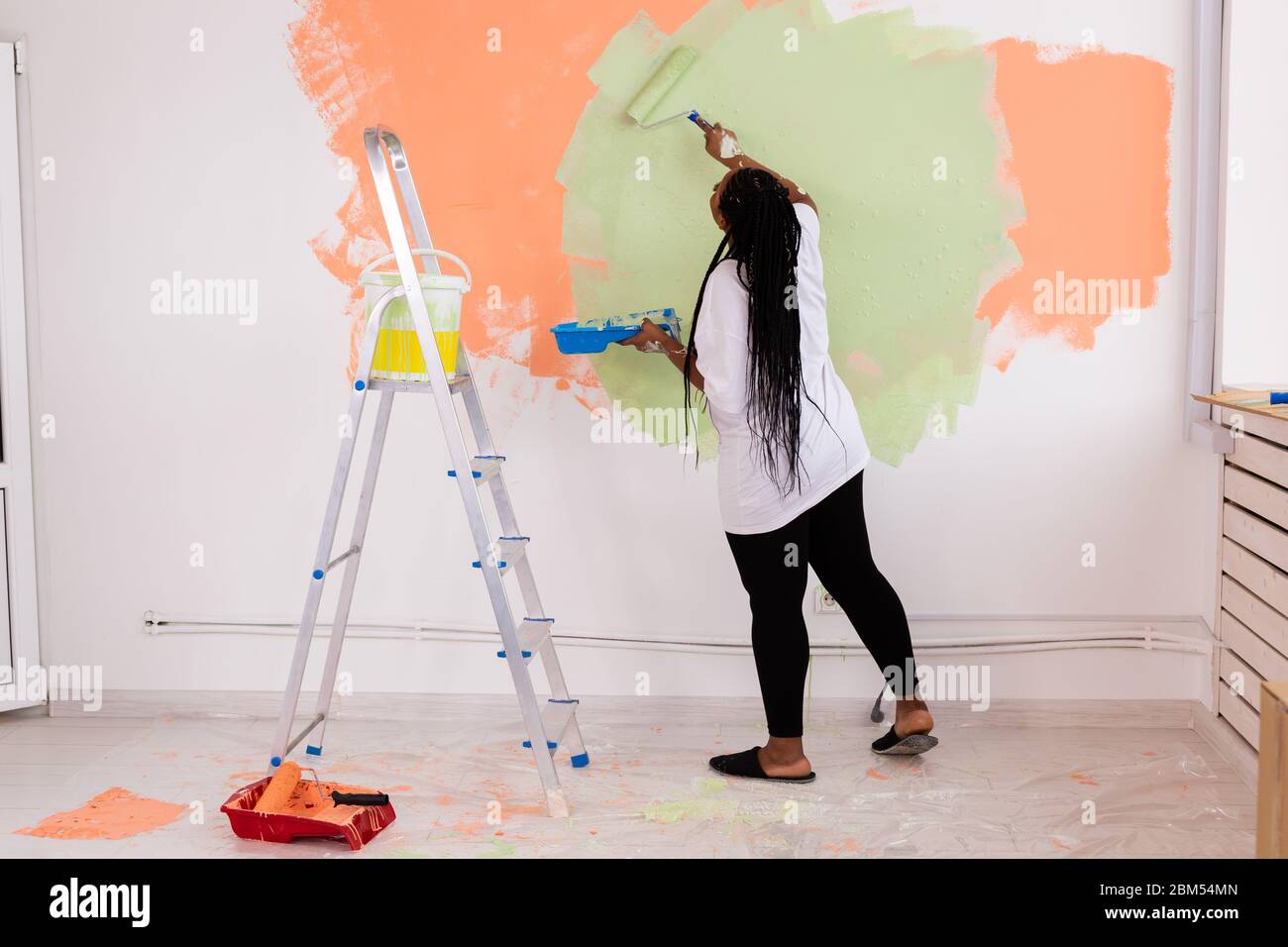 Beautiful african american girl painting the wall with paint roller. Portrait of a young ...